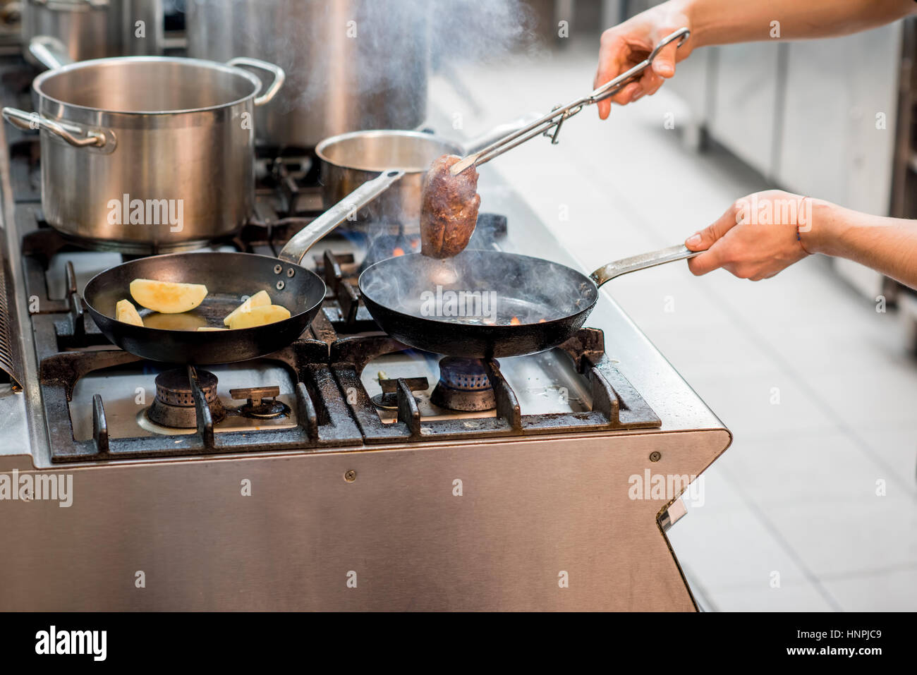 Chef frying meat steak on the gas stove at the kitchen. Close-up view ...