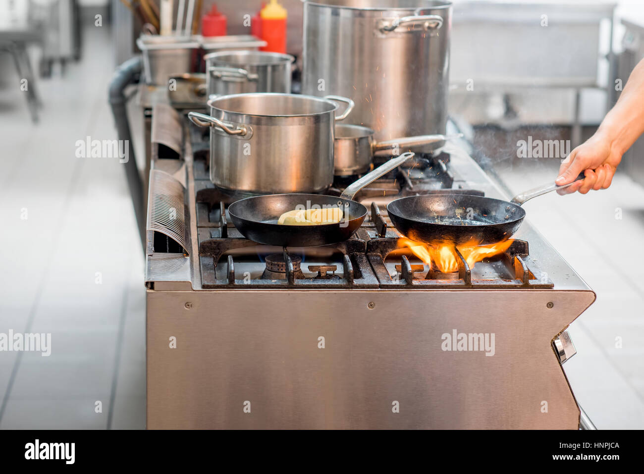 Chef frying meat steak on the gas stove with fire at the kitchen. Close ...