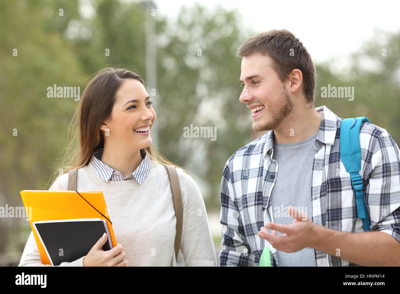 Two happy students walking towards camera and talking in a park or ...