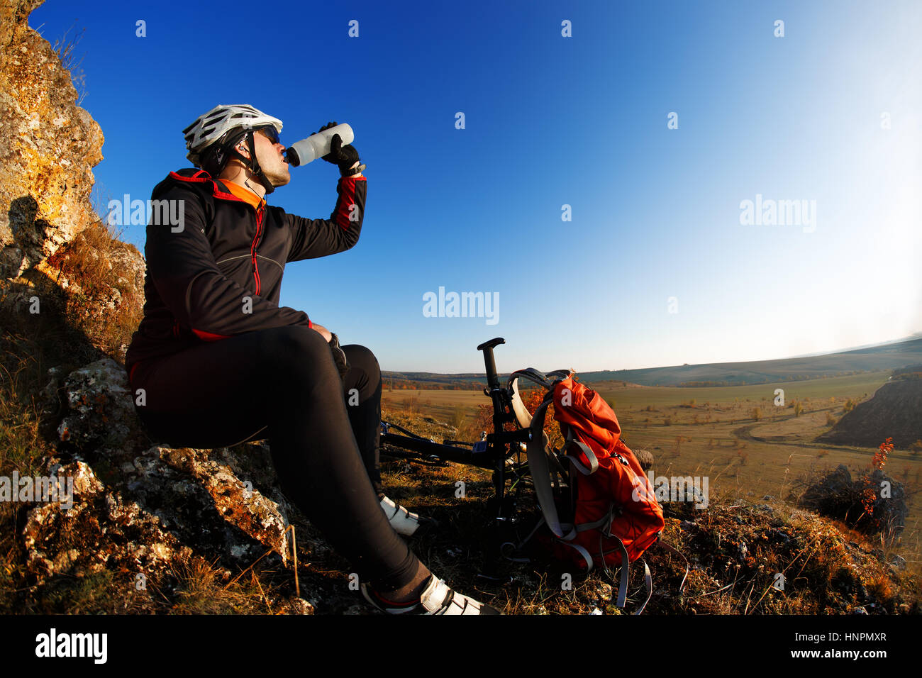 Cross country biker drinking water with bike, sky background. side view ...