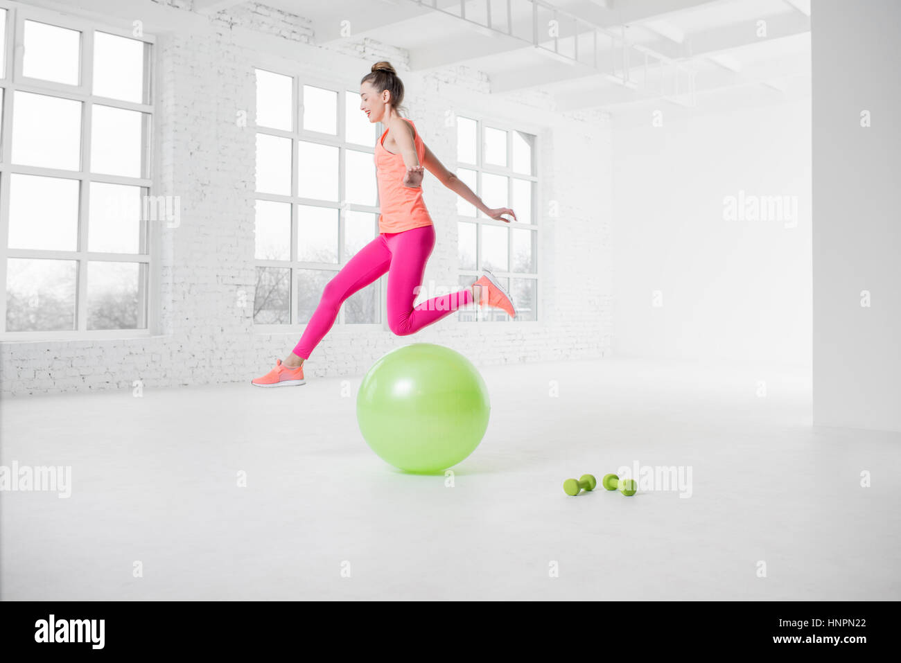 Young woman in colorful sportswear jumping over the fitness ball in the ...