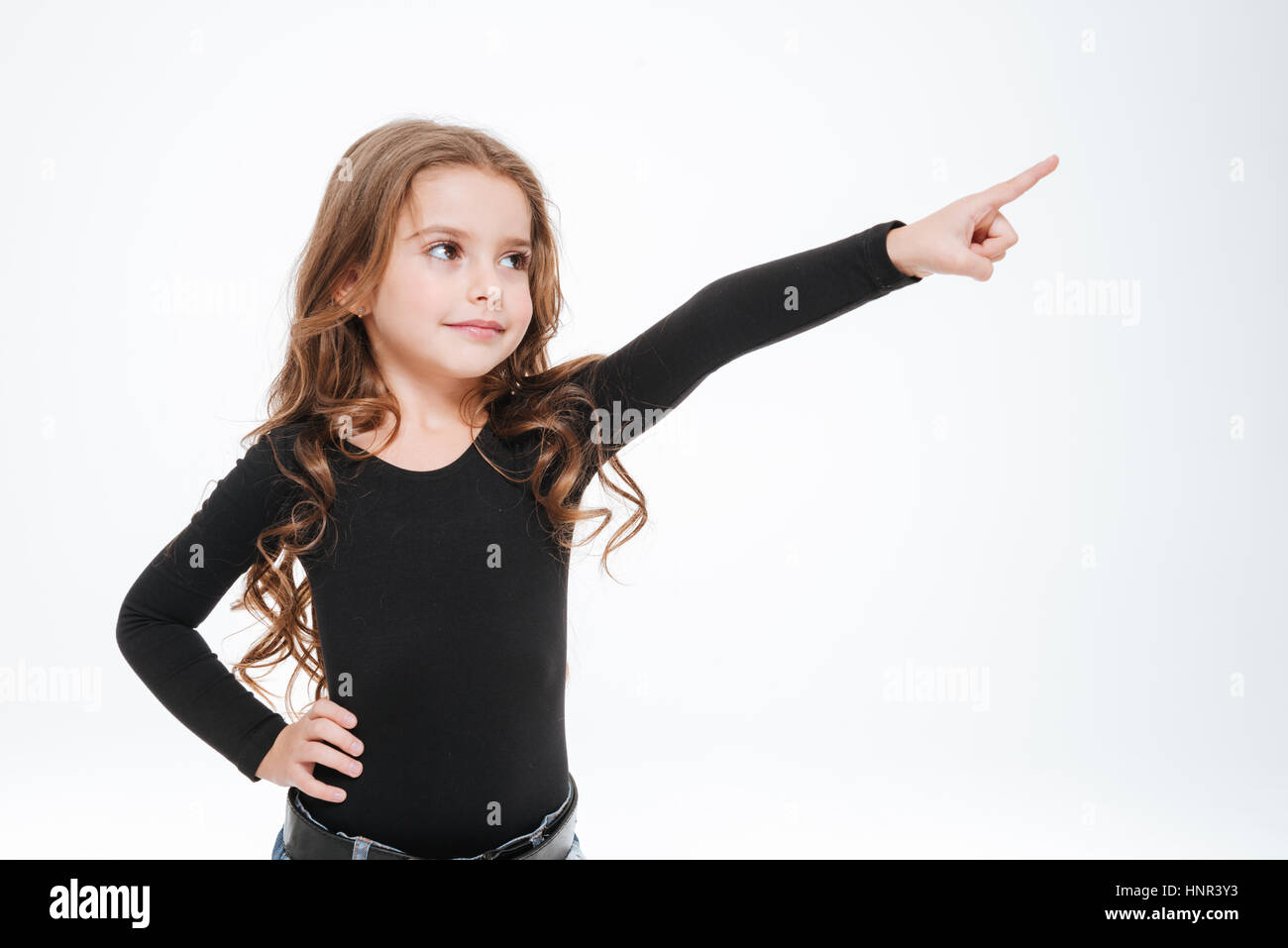 Pretty curly little girl standing and pointing away over white ...