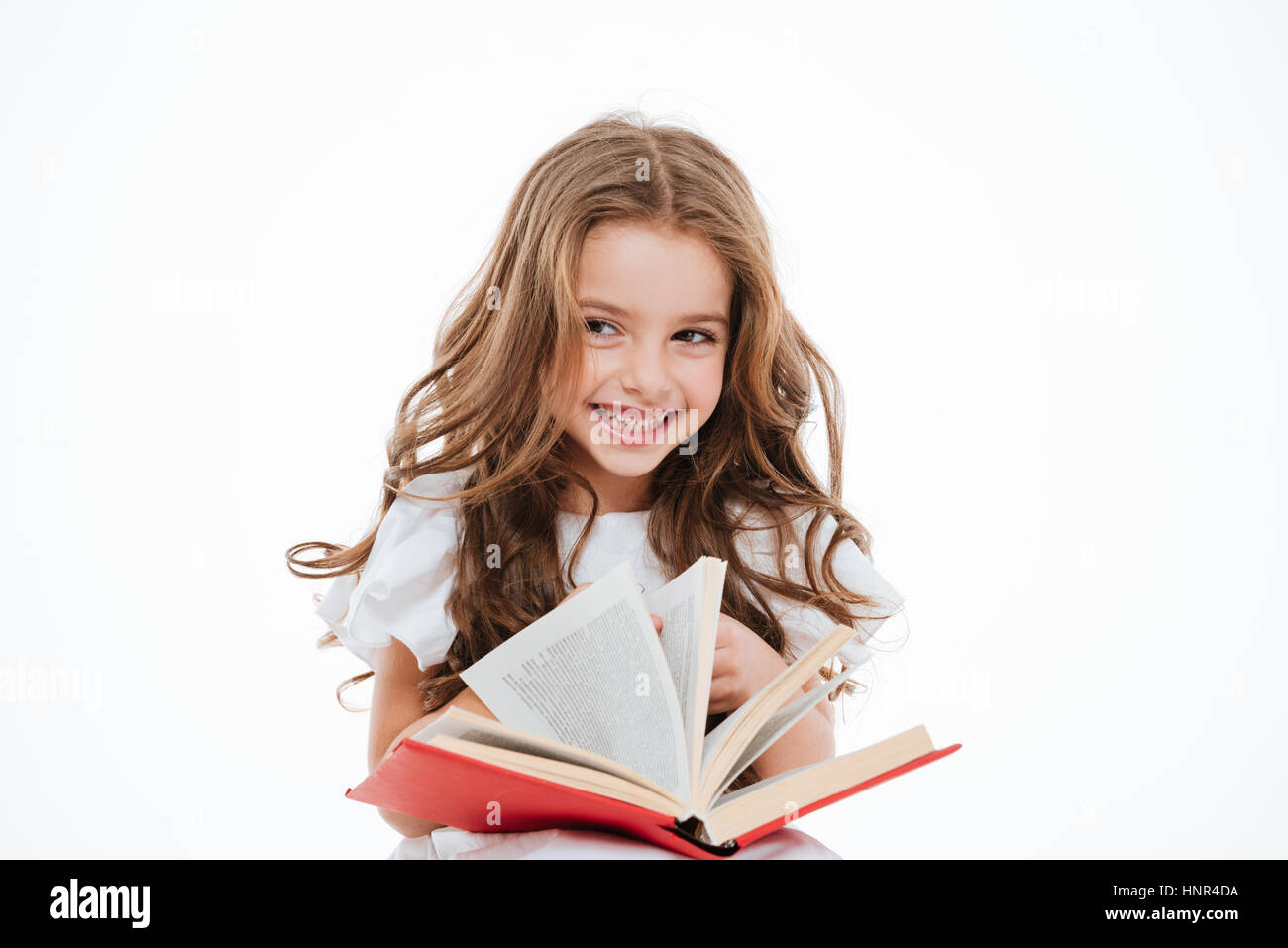 Cheerful little girl laughing and reading book over white background ...