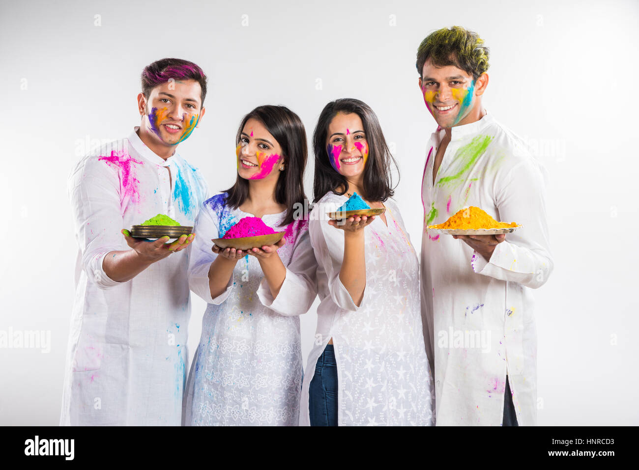 4 smart young indian people celebrating holi, standing isolated over ...