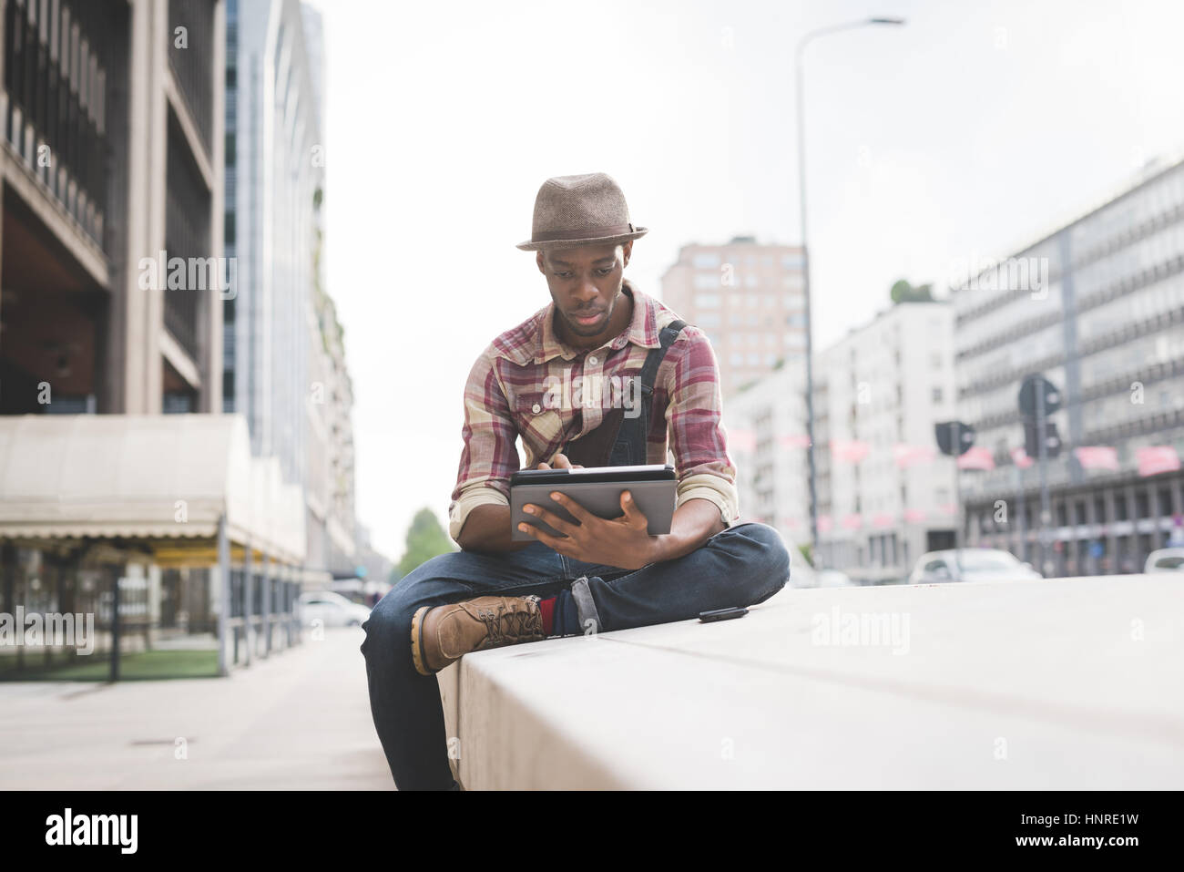 Young handsome afro black man outdoor in the city sitting using tablet - technology, social ...