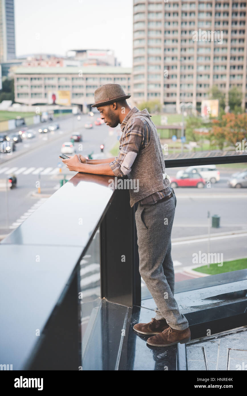 young handsome afro black man sitting on a handrail outdoorusing smart phone - technology ...