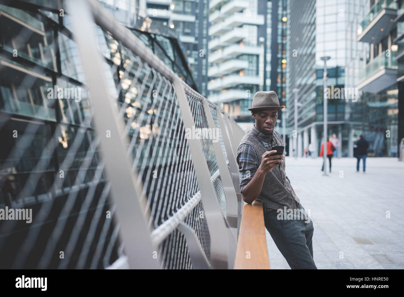 young handsome afro black man sitting on a handrail outdoorusing smart phone - technology ...