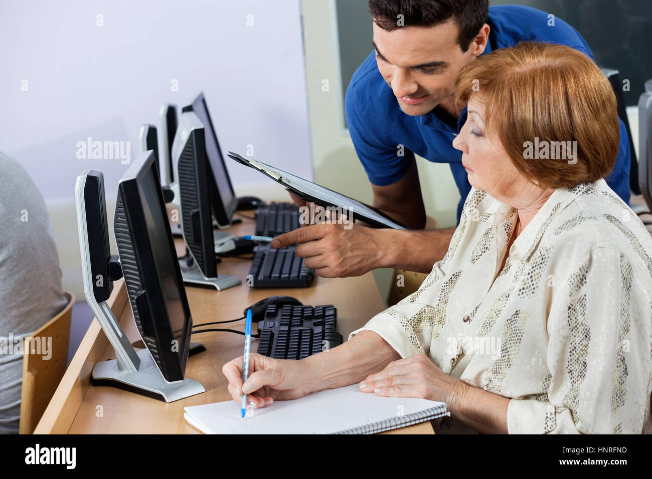 Computer Tutor Holding Clipboard While Senior Woman Writing Note Stock ...