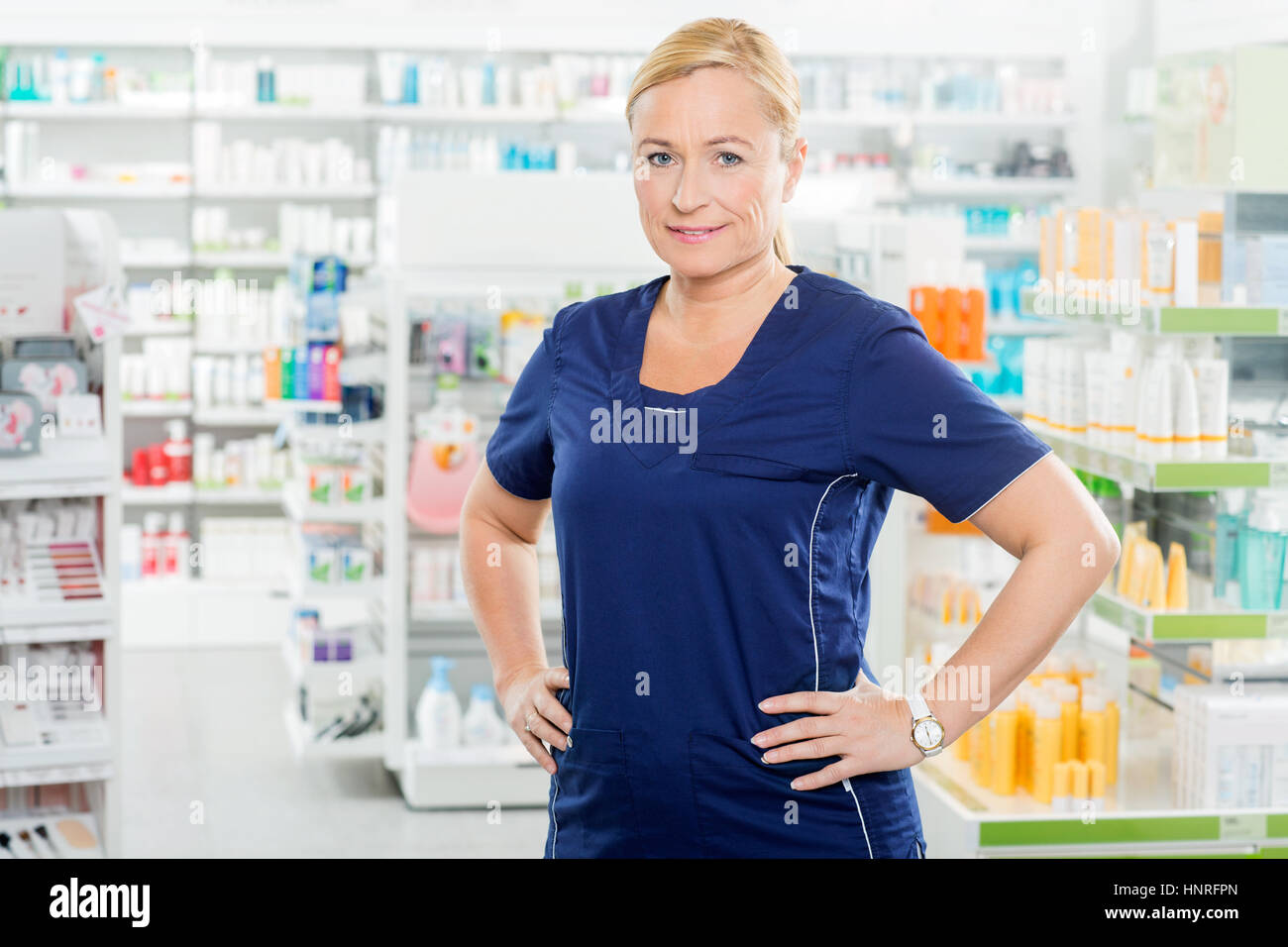 Female Chemist Standing With Hands On Hip In Pharmacy Stock Photo - Alamy