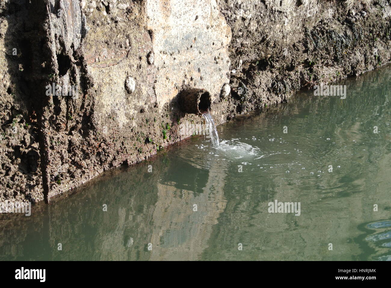 small stone pipe mounted in harbor wall discharging water into the sea ...