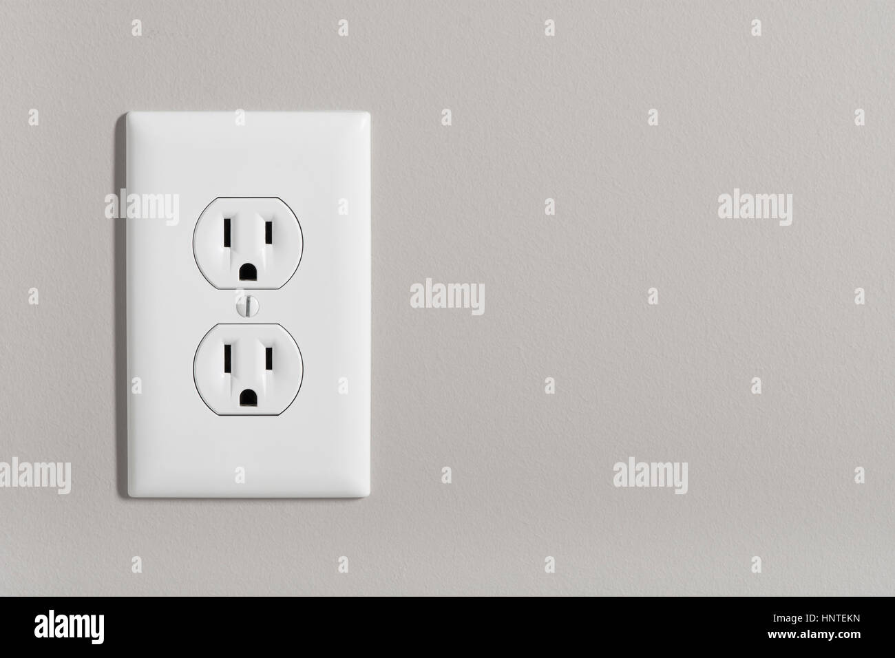A white home electrical outlet on a light grey wall Stock Photo - Alamy