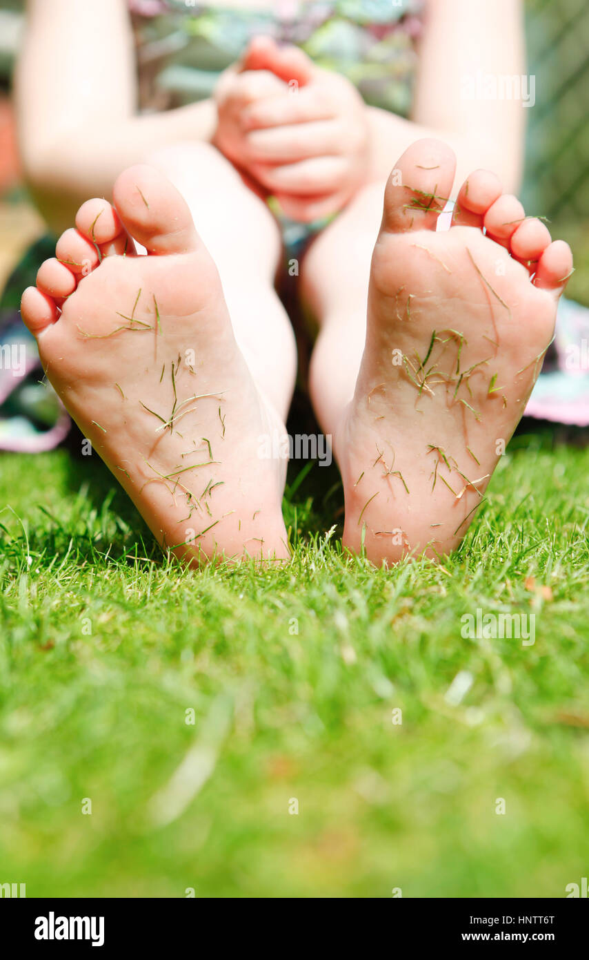 Four year old girl in a garden with grass cuttings on the soles of her ...