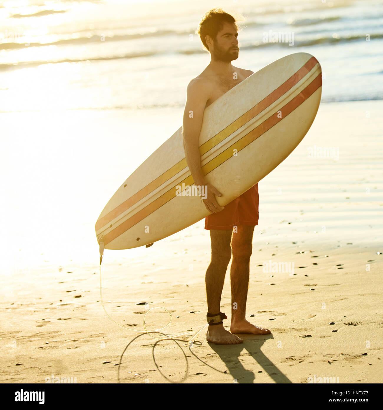 Square image of surfer holding a surfboard under his arm Stock Photo ...
