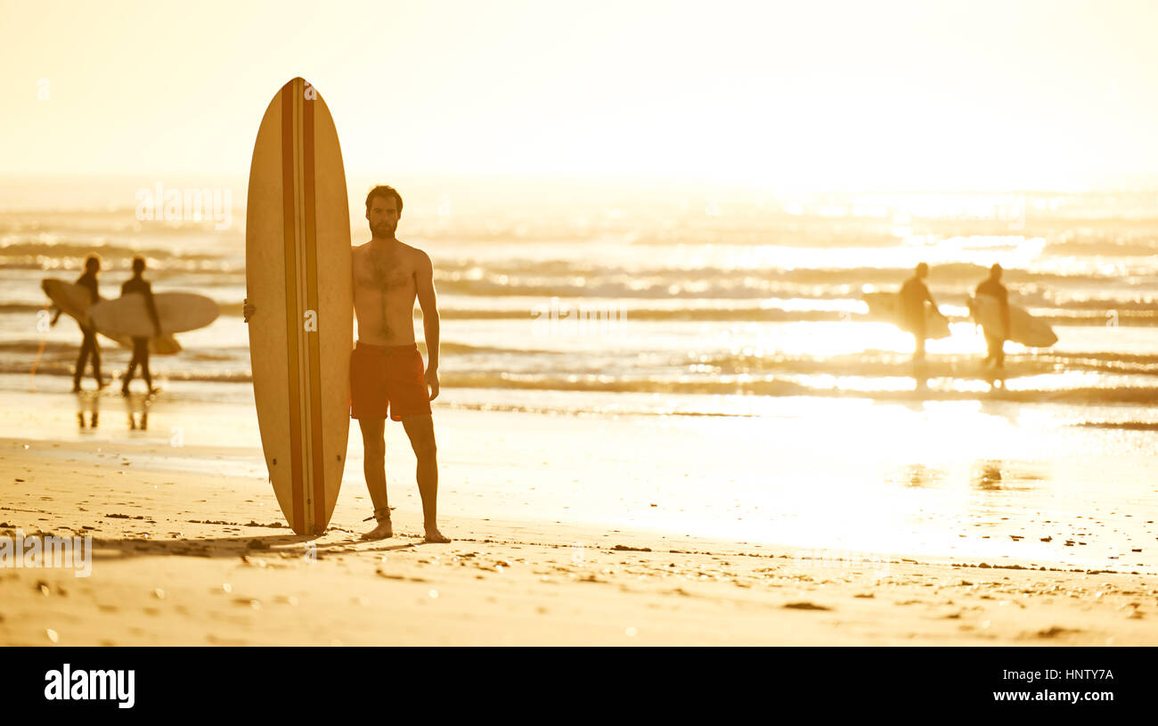Surfer standing on beach with other surfers behind him Stock Photo - Alamy