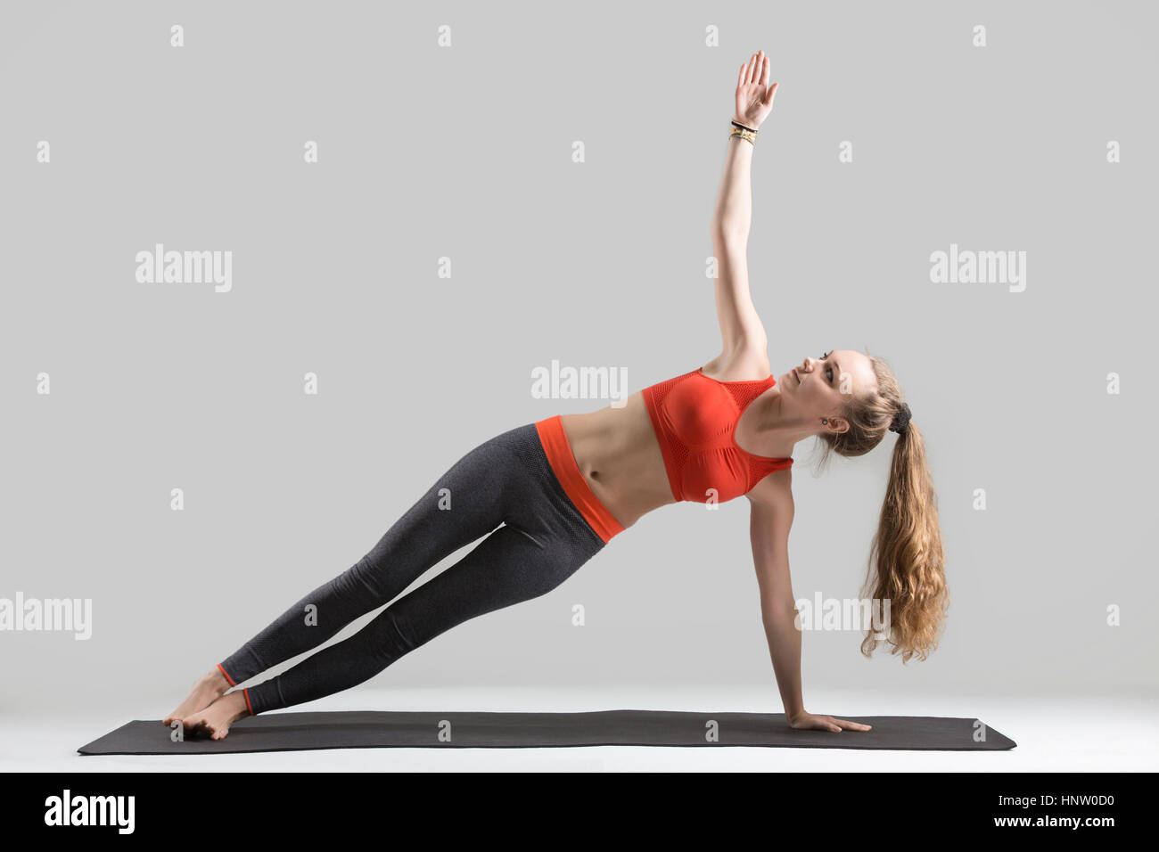 Young attractive woman standing in Side Plank pose, grey studio Stock ...