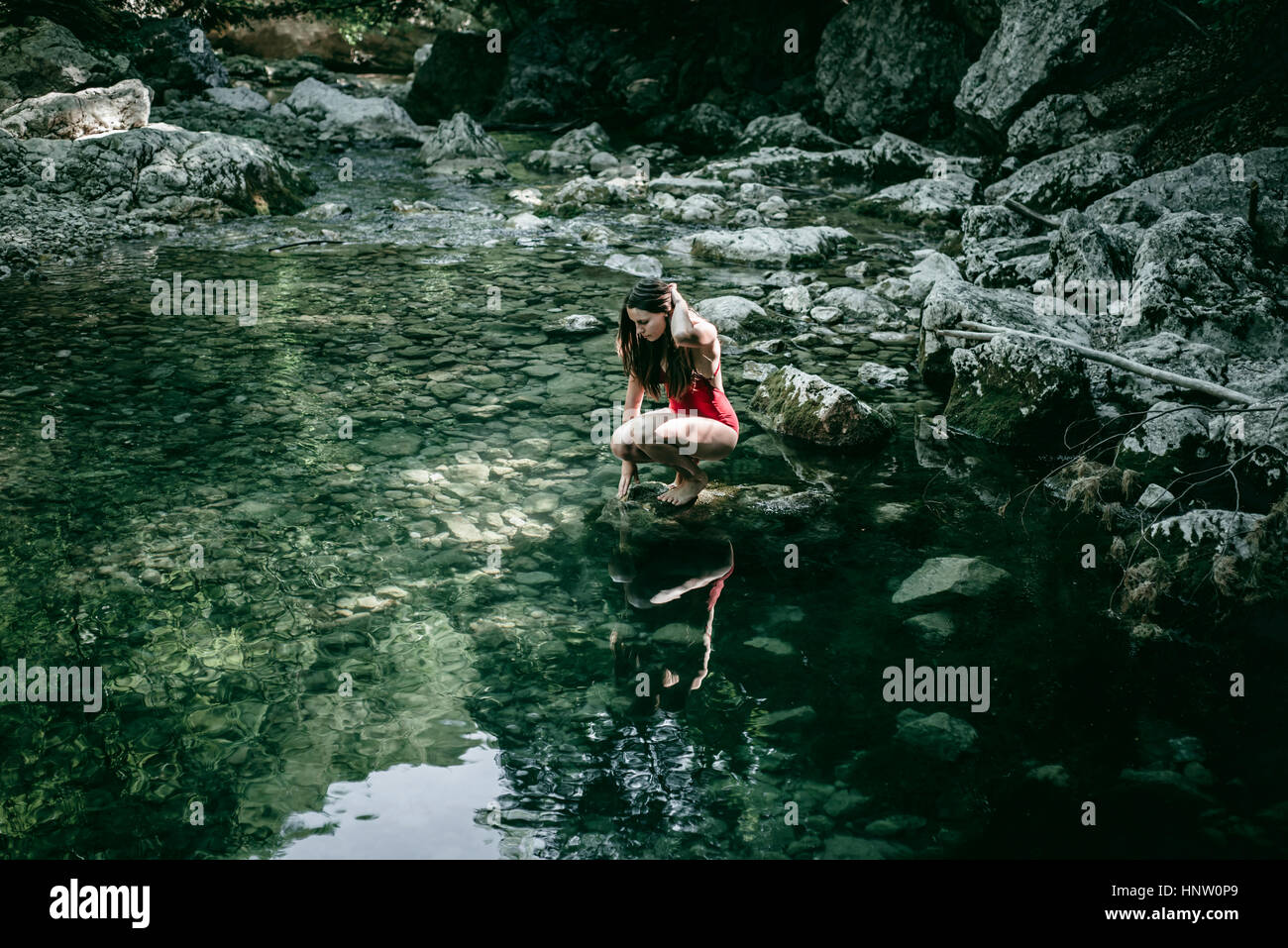 Caucasian woman crouching on rocks at pool of water Stock Photo - Alamy