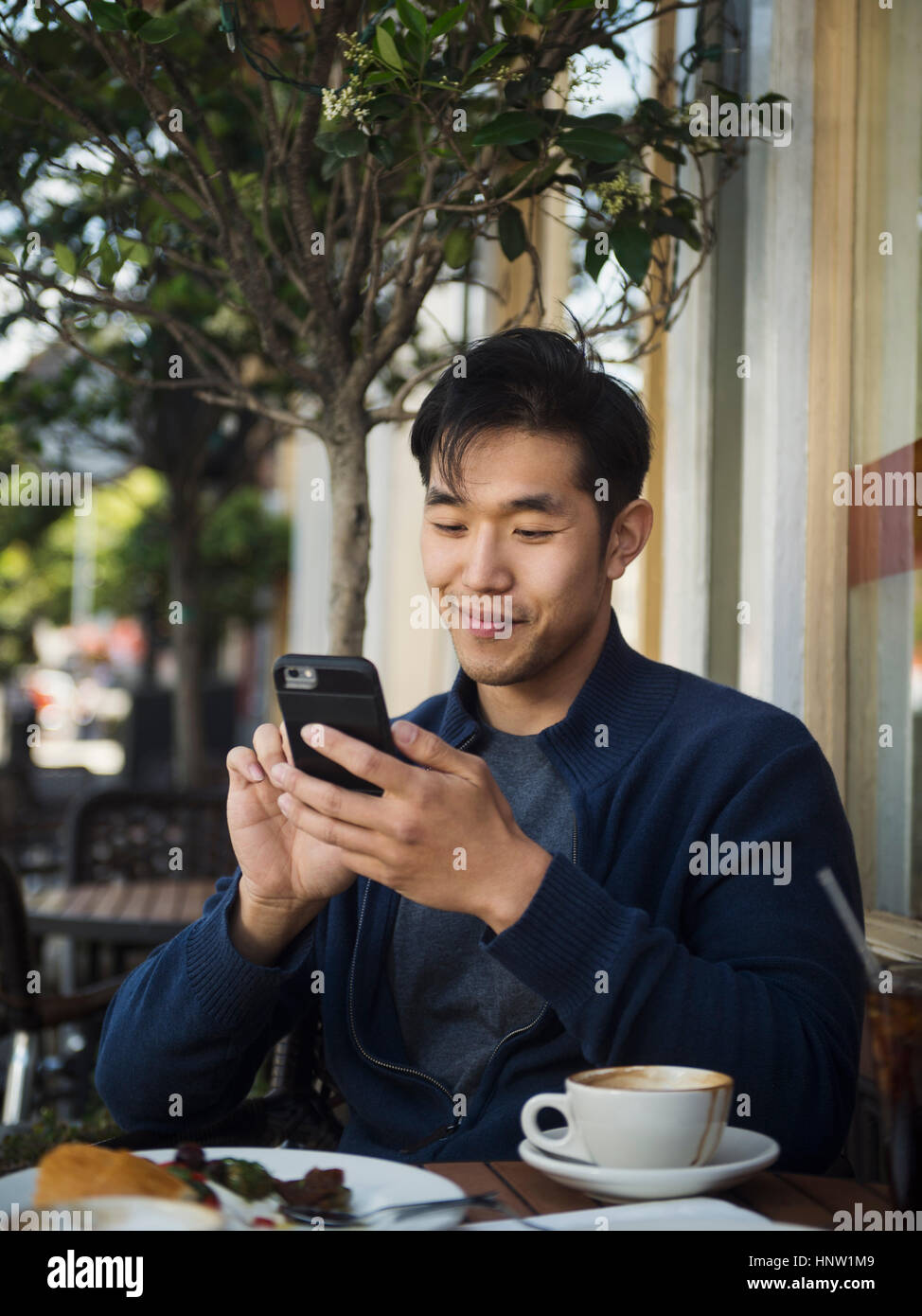 Smiling Chinese man texting on cell phone at outdoor cafe Stock Photo ...