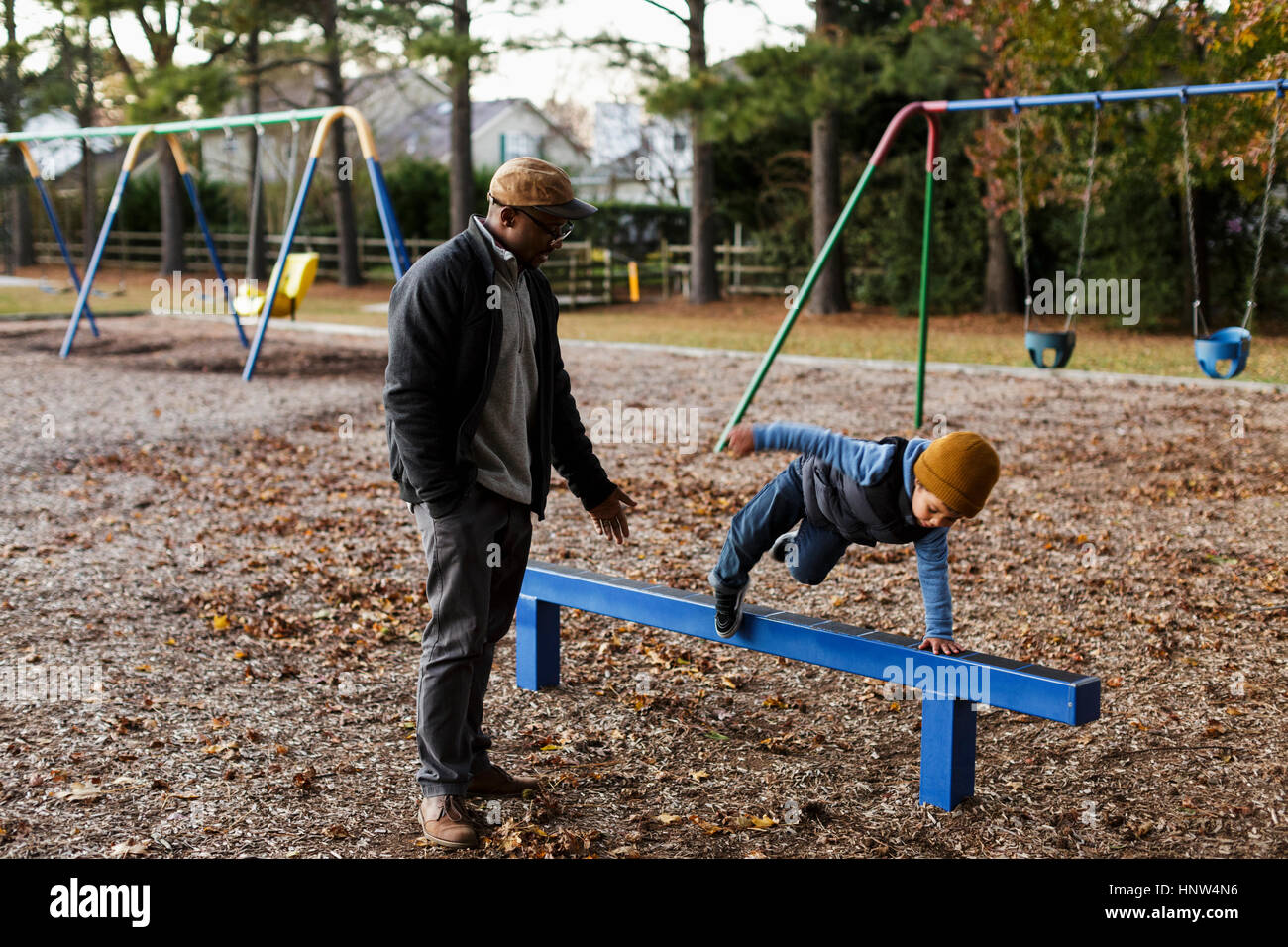 Father watching son jumping over playground beam Stock Photo - Alamy