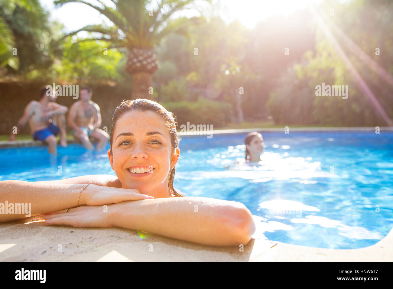 Woman in swimming pool resting on poolside looking at camera smiling ...