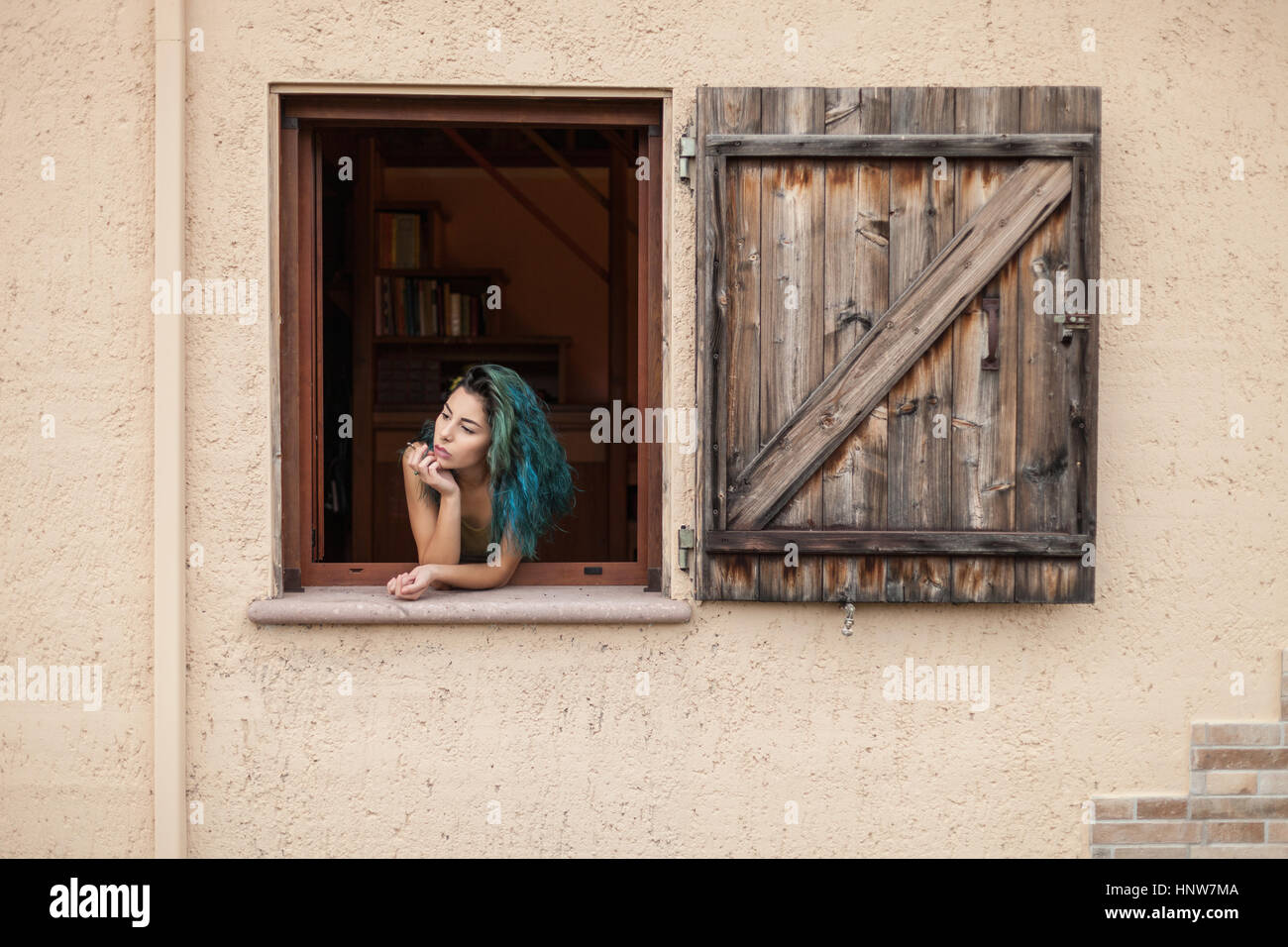 Young woman with blue hair, looking out of open window Stock Photo - Alamy