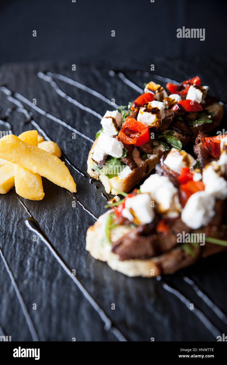 Meat, feta and tomato open sandwiches with chips and sauce garnish on ...
