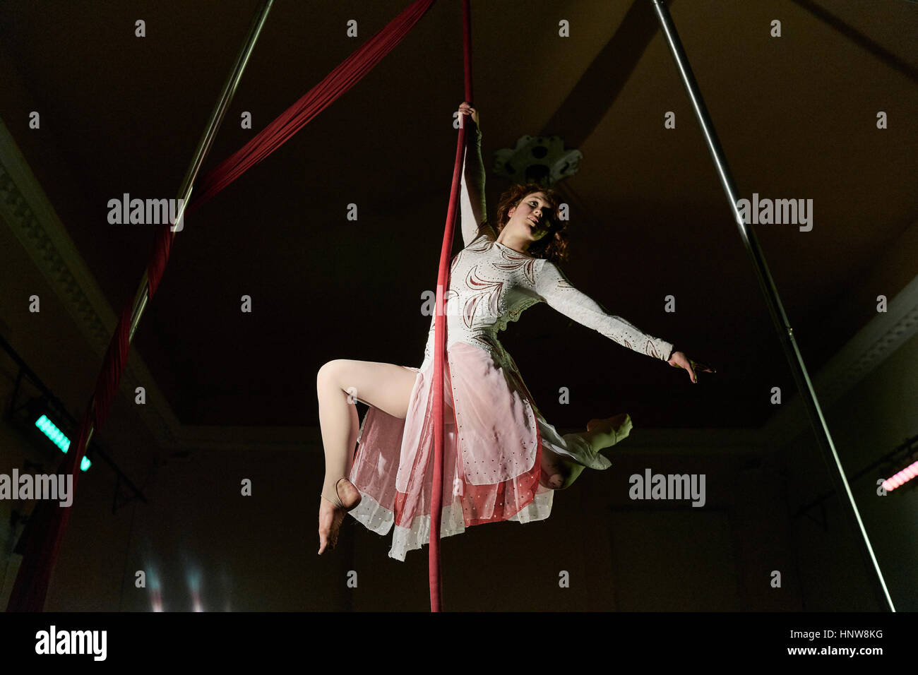 Low angle view of young female aerial acrobat hanging from silk rope ...