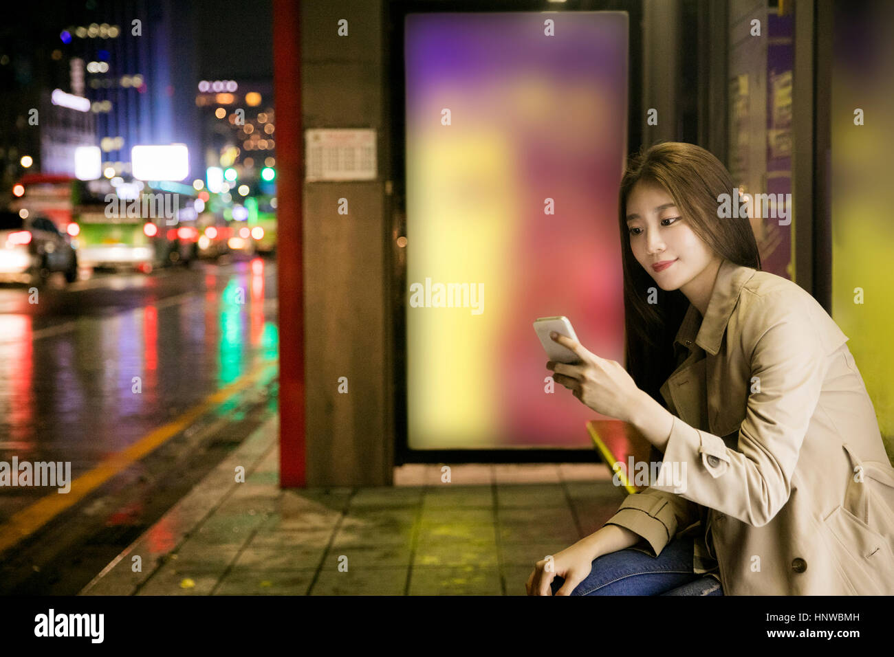 Young woman using smartphone at bus stop Stock Photo - Alamy