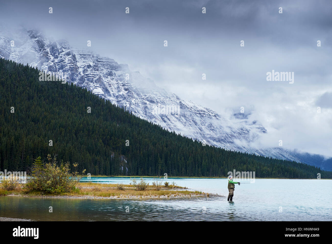 Man fly fishing in lake by snow capped mountains, Banff, Alberta ...