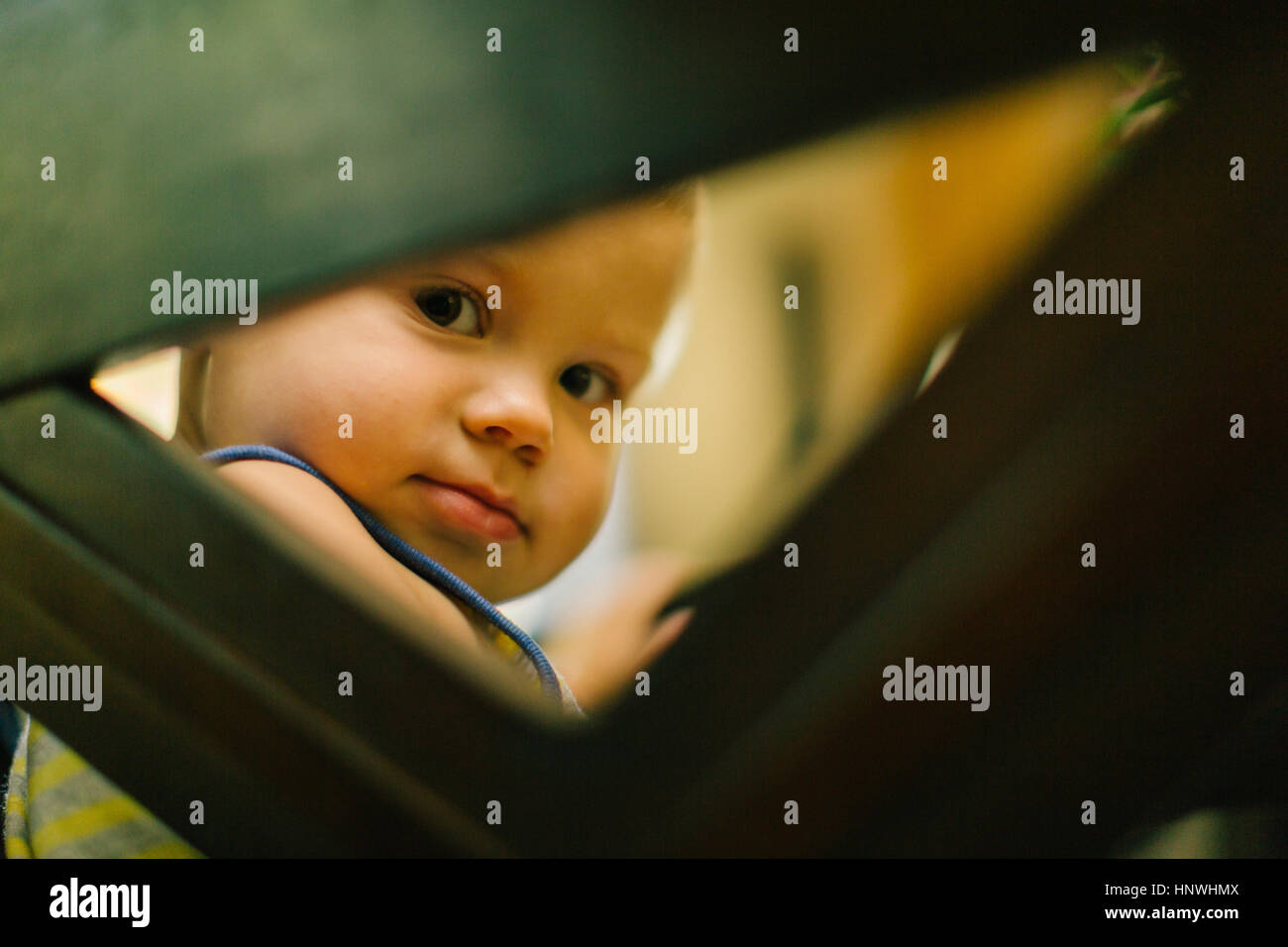 Young boy looking through gap in furniture Stock Photo - Alamy