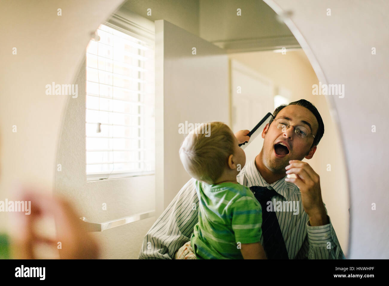 Father holding young son, son trying to comb father's hair, reflected ...