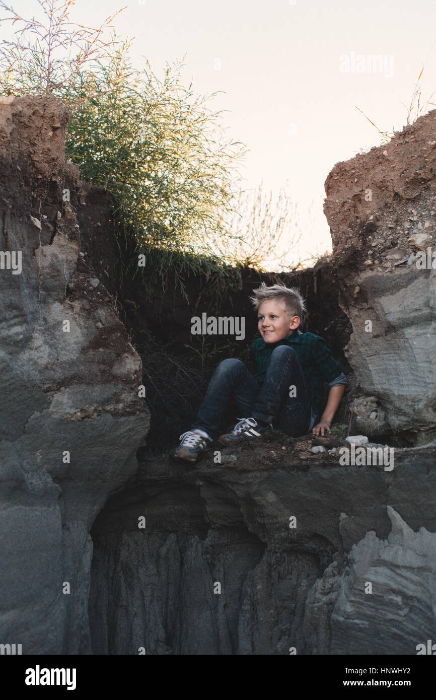 Boy hiding on ledge below cliff edge Stock Photo - Alamy