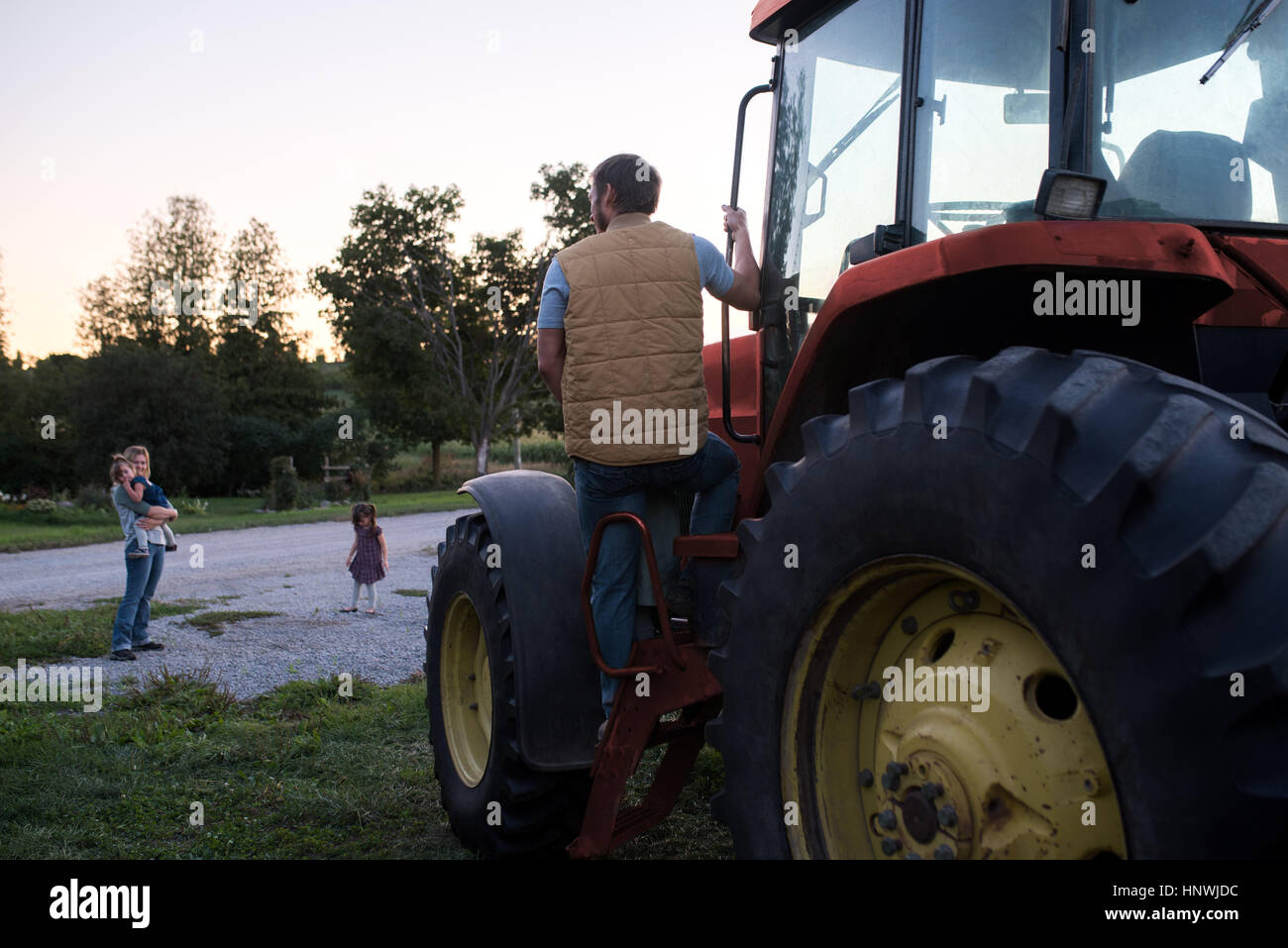 Family on farm, father climbing into tractor Stock Photo - Alamy