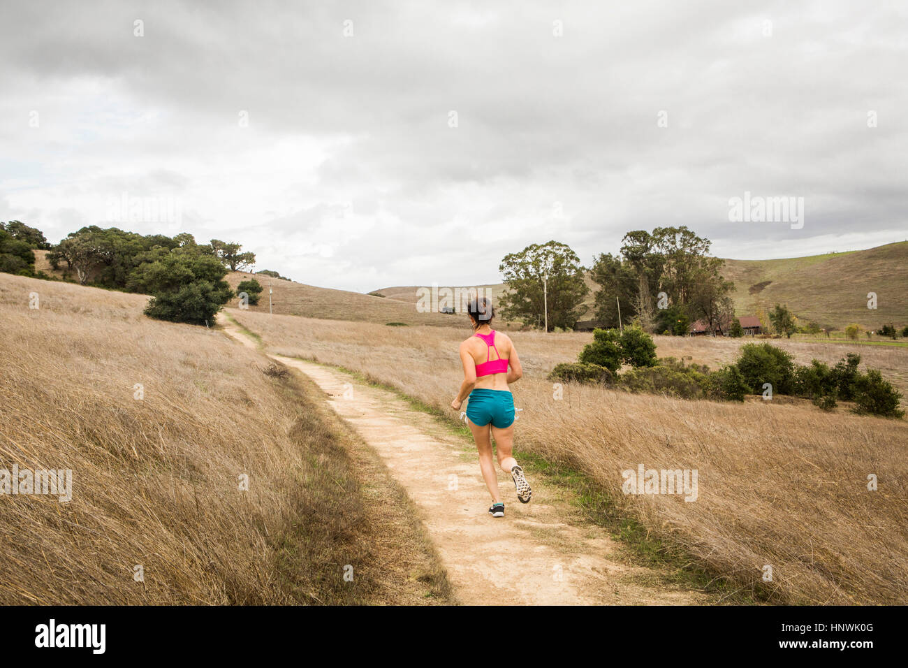 Rear view of female runner running on dirt track in landscape Stock ...