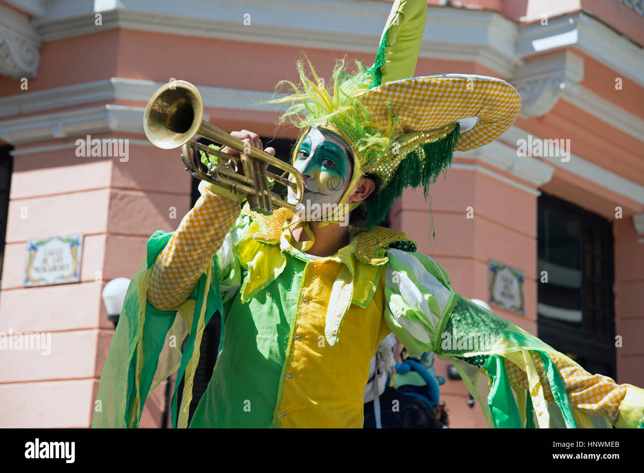 A street musician dressed in a jester costume plays his trumpet outside ...