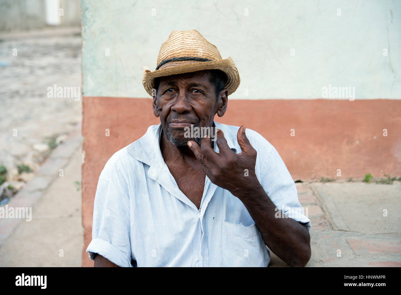 Portrait of an old Cuban man wearing a straw hat sits on the corner of ...
