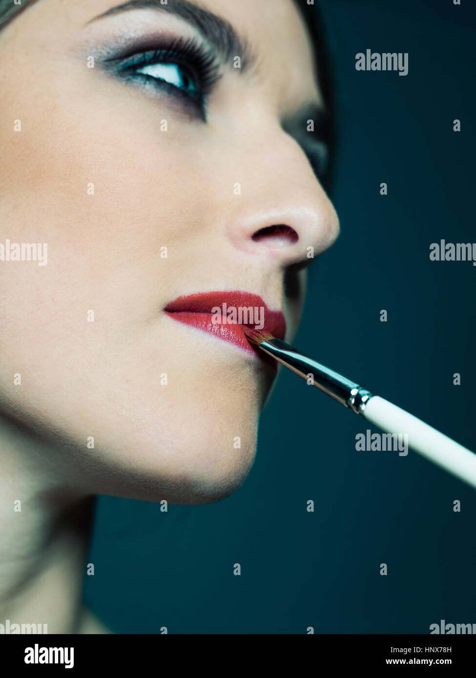Side view of red lipstick being applied to lip of beautiful young woman ...