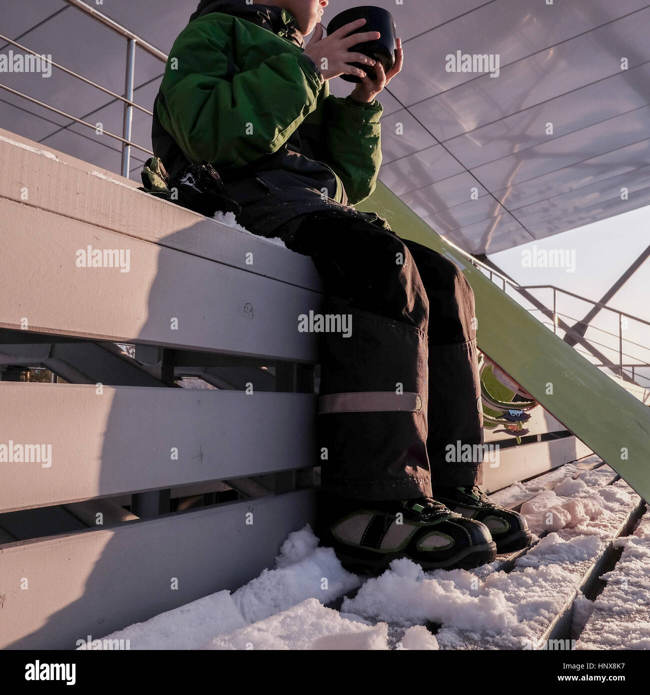Cropped view of boy wearing ski suit sitting on bench Stock Photo - Alamy