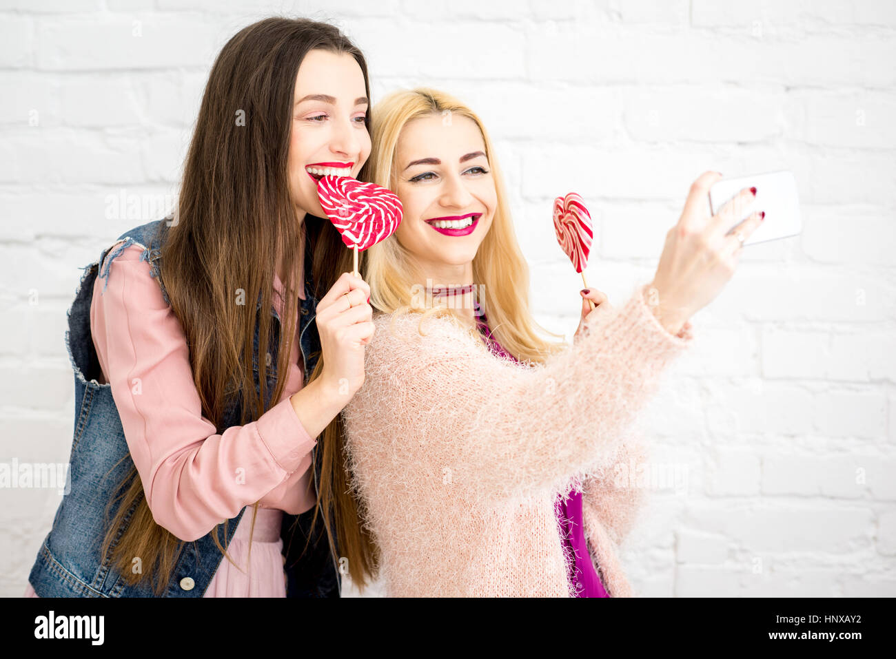 Female stylish friends making selfie photo with red candies on the ...