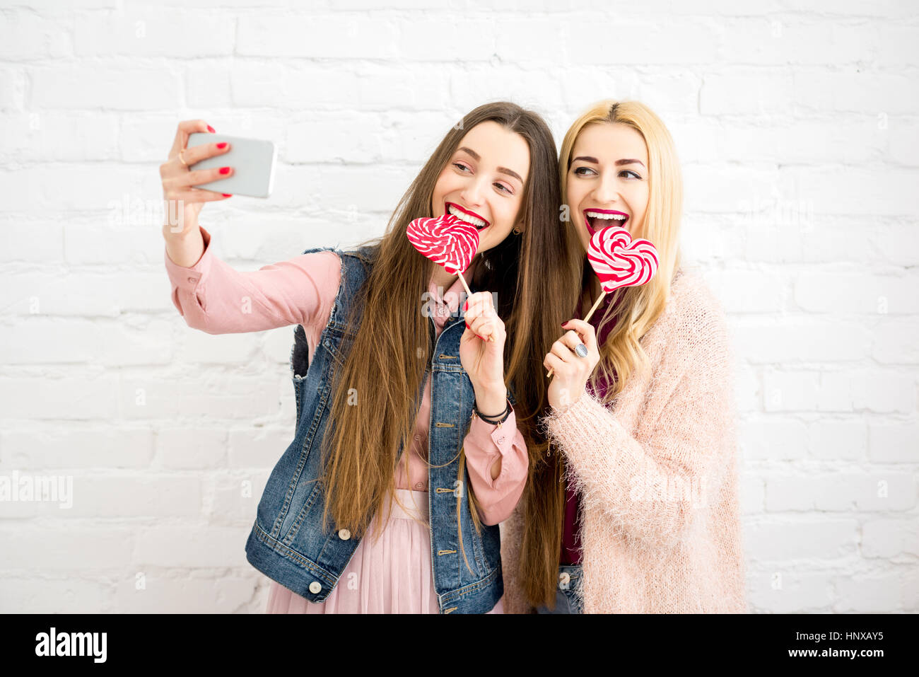 Female stylish friends making selfie photo with red candies on the ...