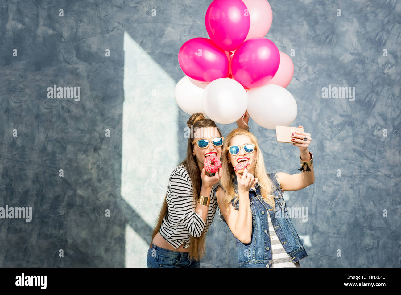 Playful women having fun with sweet donuts and baloons on the blue wall ...