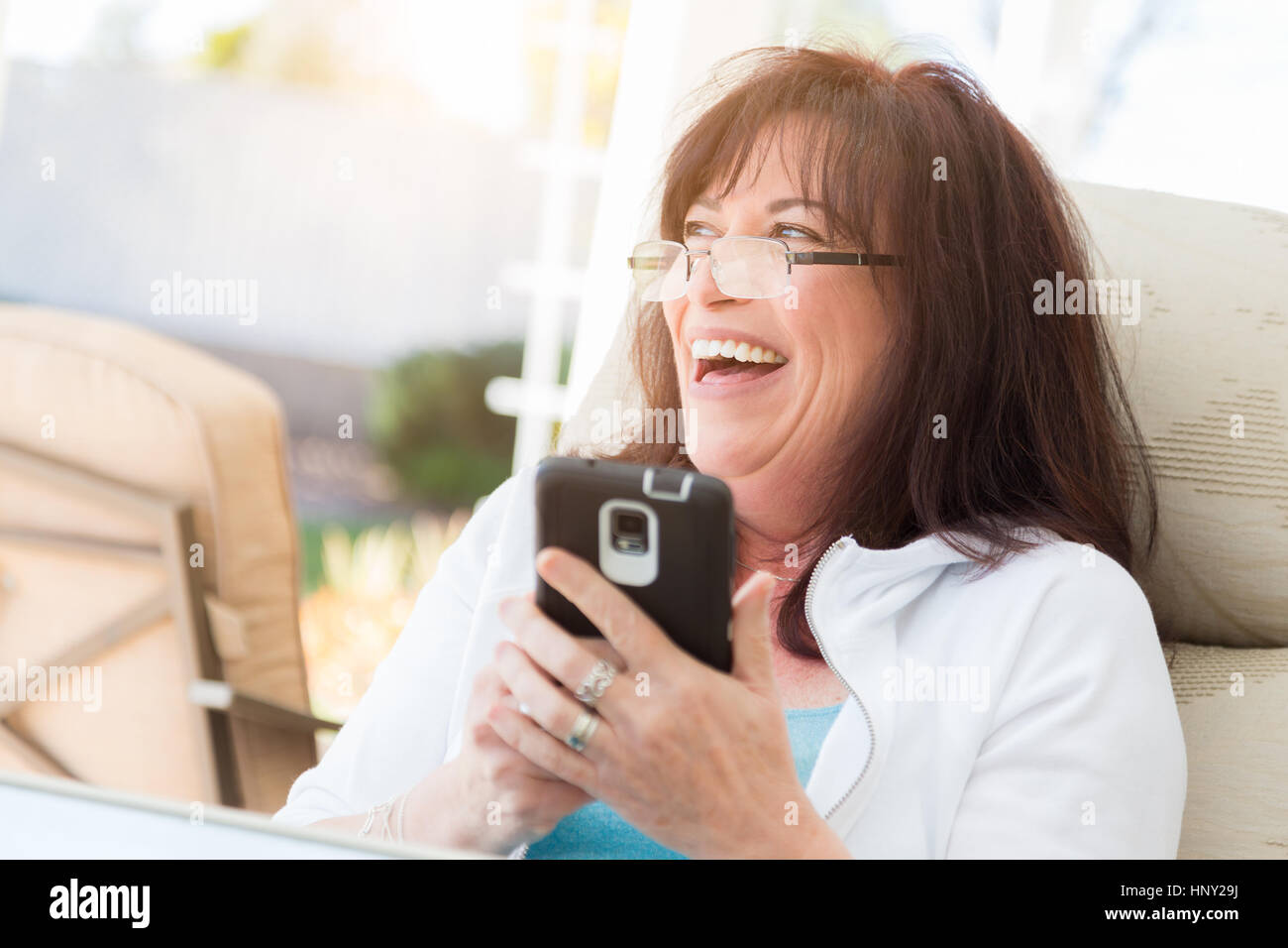 Attractive Middle Aged Woman Laughing While Using Her Smart Phone On The Patio Stock Photo - Alamy