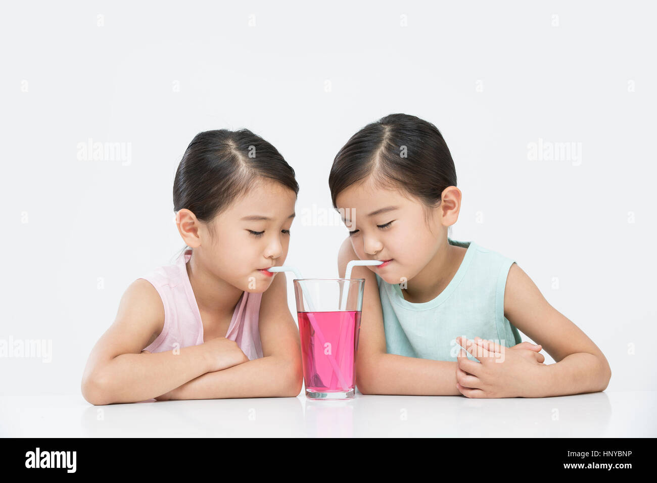Smiling twin girls sharing juice Stock Photo - Alamy