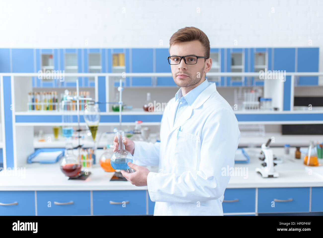 scientist in eyeglasses holding flask with reagent and looking at ...