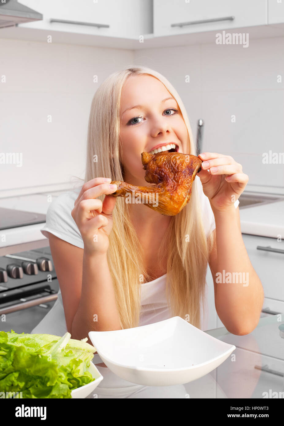 beautiful young blond woman eating chicken in the kitchen at home Stock ...
