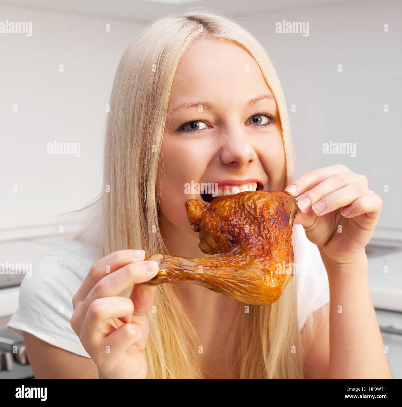 beautiful young blond woman eating chicken in the kitchen at home Stock ...