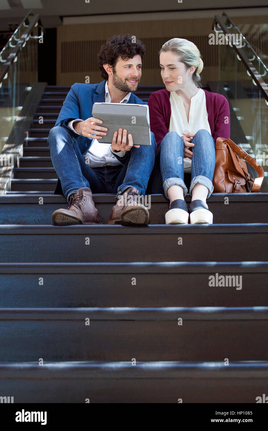 Couple sitting on steps, using digital tablet Stock Photo - Alamy