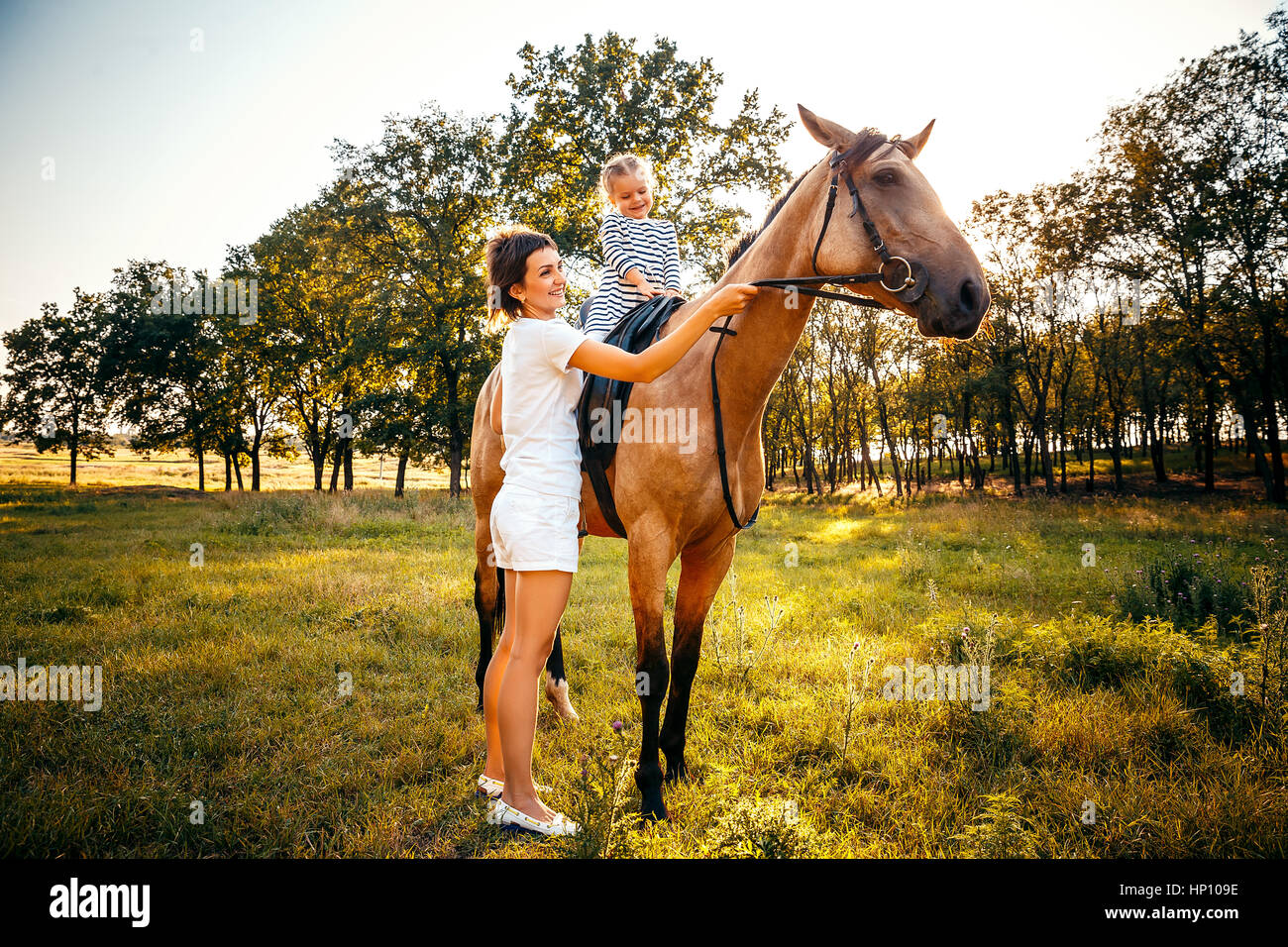 Little girl riding on a horseback with her mother standing nearby Stock ...