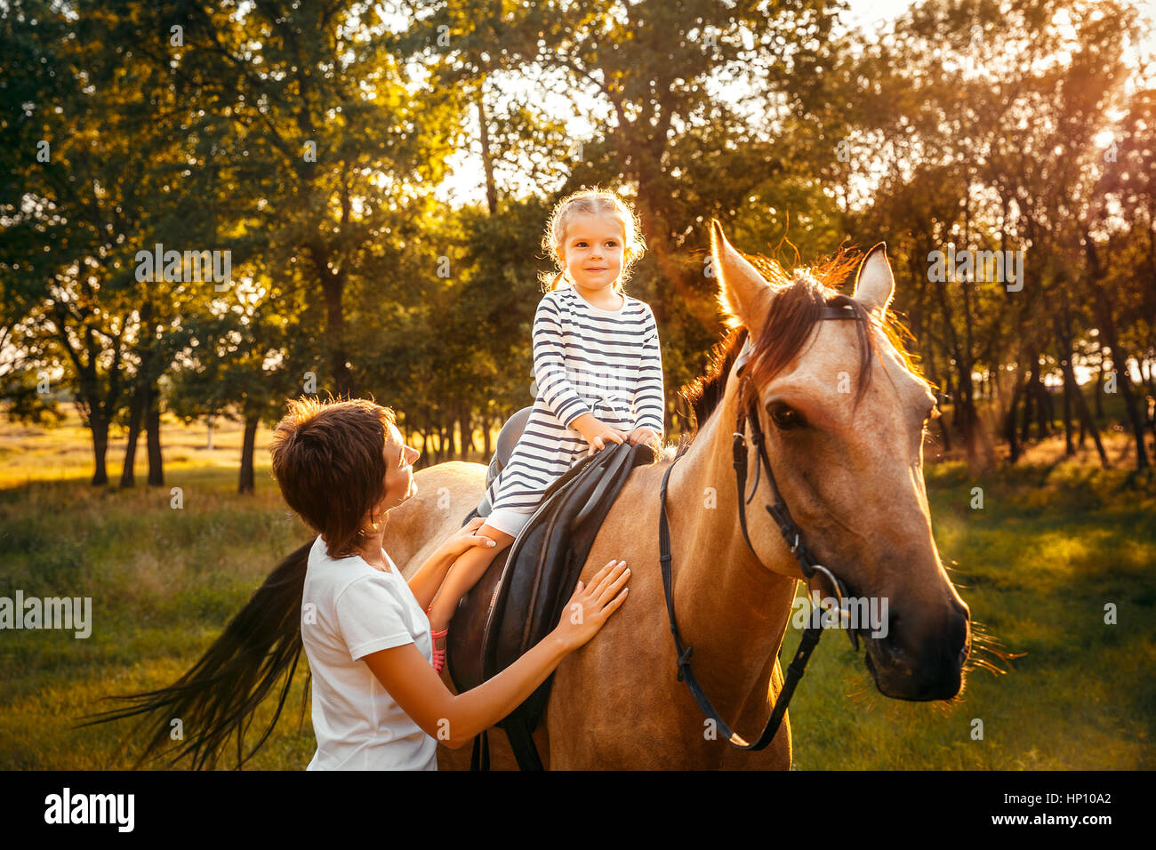 Little girl riding on a horseback with her mother standing nearby Stock ...