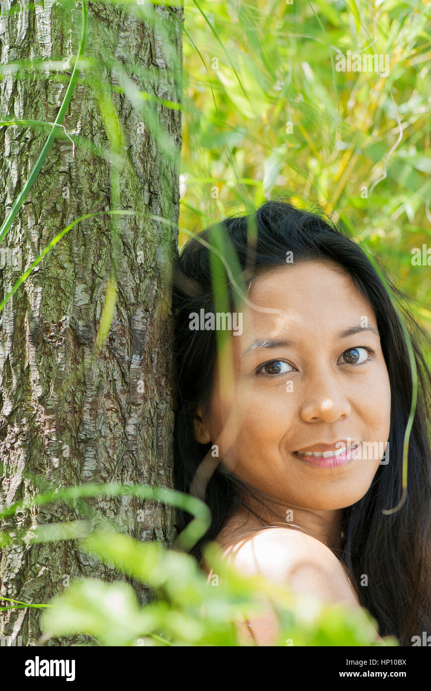 Woman leaning against tree trunk, portrait Stock Photo - Alamy
