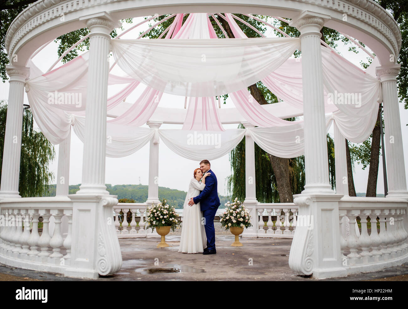 Wedding couple under large arch with pink material decoration with ...